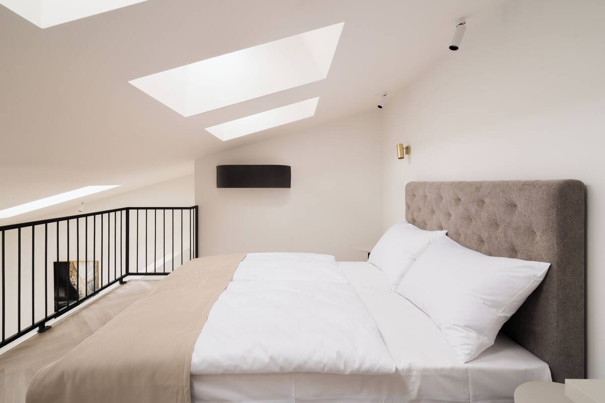Quarto com cama, cabeceira, janela e luminária fixada na parede.