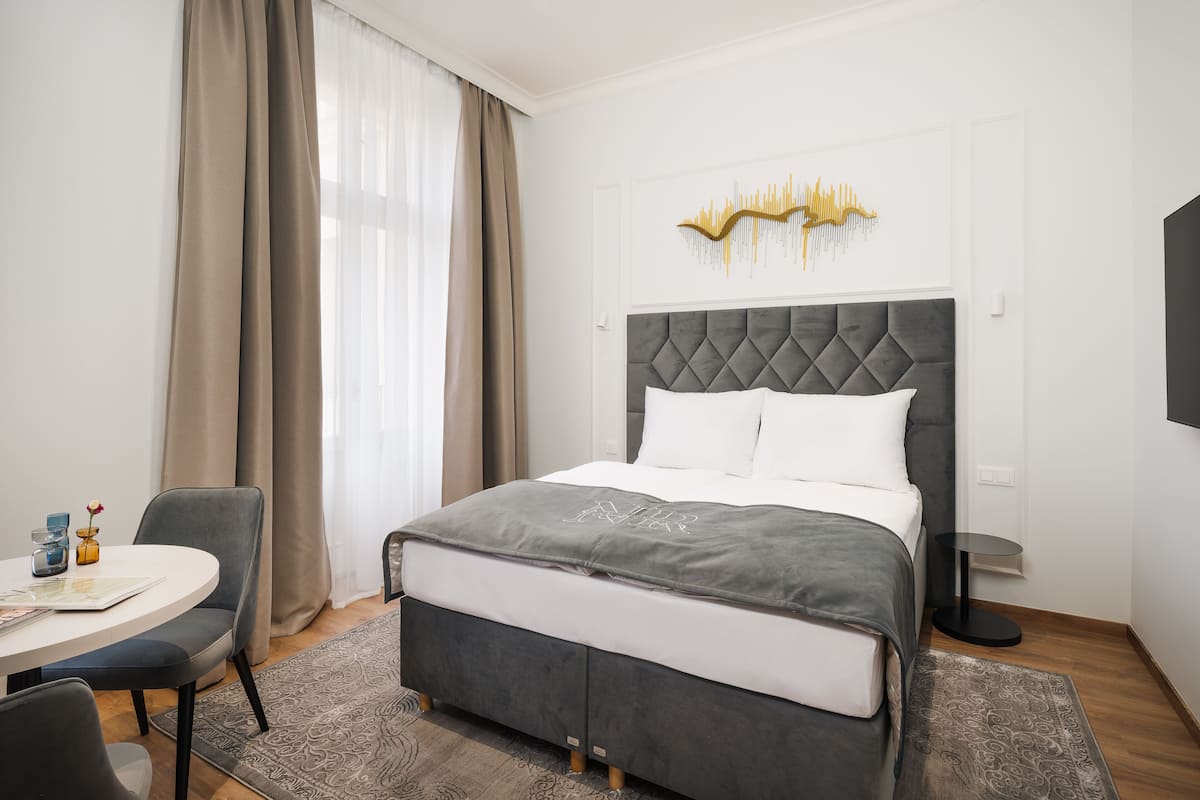 Quarto de hotel moderno com uma cama grande, uma mesa de jantar redonda e uma pequena mesinha lateral.