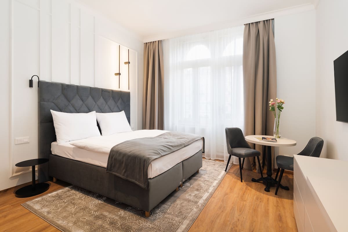 Quarto de hotel moderno com uma cama grande, uma mesinha redonda, duas cadeiras e uma escrivaninha.