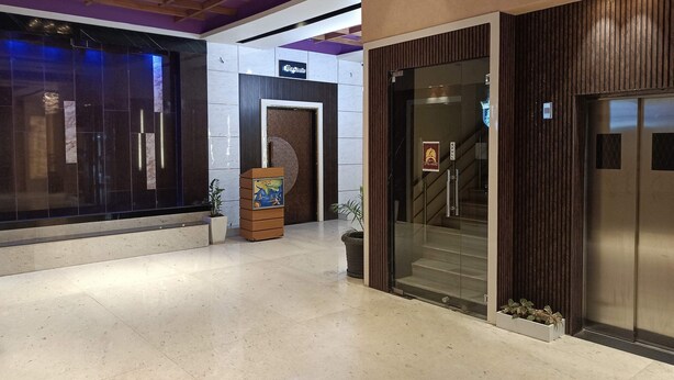 Um hall moderno com elevador de vidro, um balcão de recepção e uma escada.