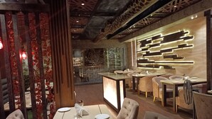 Restaurante com decoração moderna, apresentando uma área de jantar central com mesas e cadeiras, uma parede decorativa com padrão de girafa e um bar com divisória de vidro.