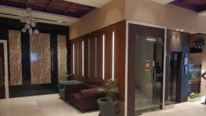 Um lobby moderno com parede de mármore, um sofá, uma planta em vaso e um elevador de vidro.