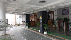 Um lobby amplo com teto alto, balcão de recepção e plantas em vasos.