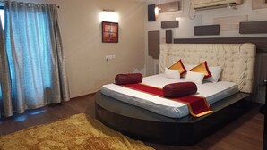 Quarto moderno com cabeceira estofada, cama grande com roupa de cama vermelha e branca, tapete amarelo e um aparelho de ar condicionado na parede.