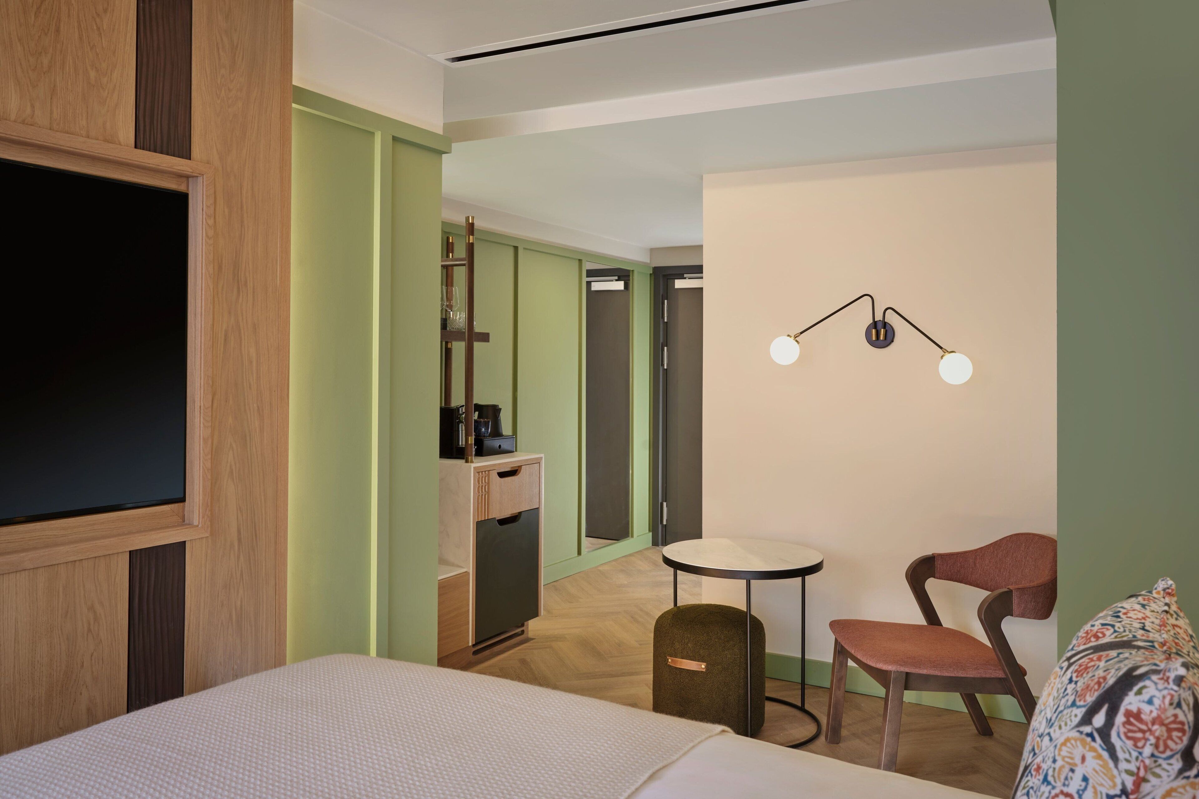Quarto de hotel com uma cama, uma mesa de escritório, uma cadeira, uma pequena mesa e um candeeiro fixado na parede.