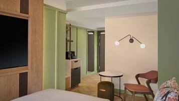 Quarto de hotel com uma cama, uma mesa de escritório, uma cadeira, uma pequena mesa e um candeeiro fixado na parede.