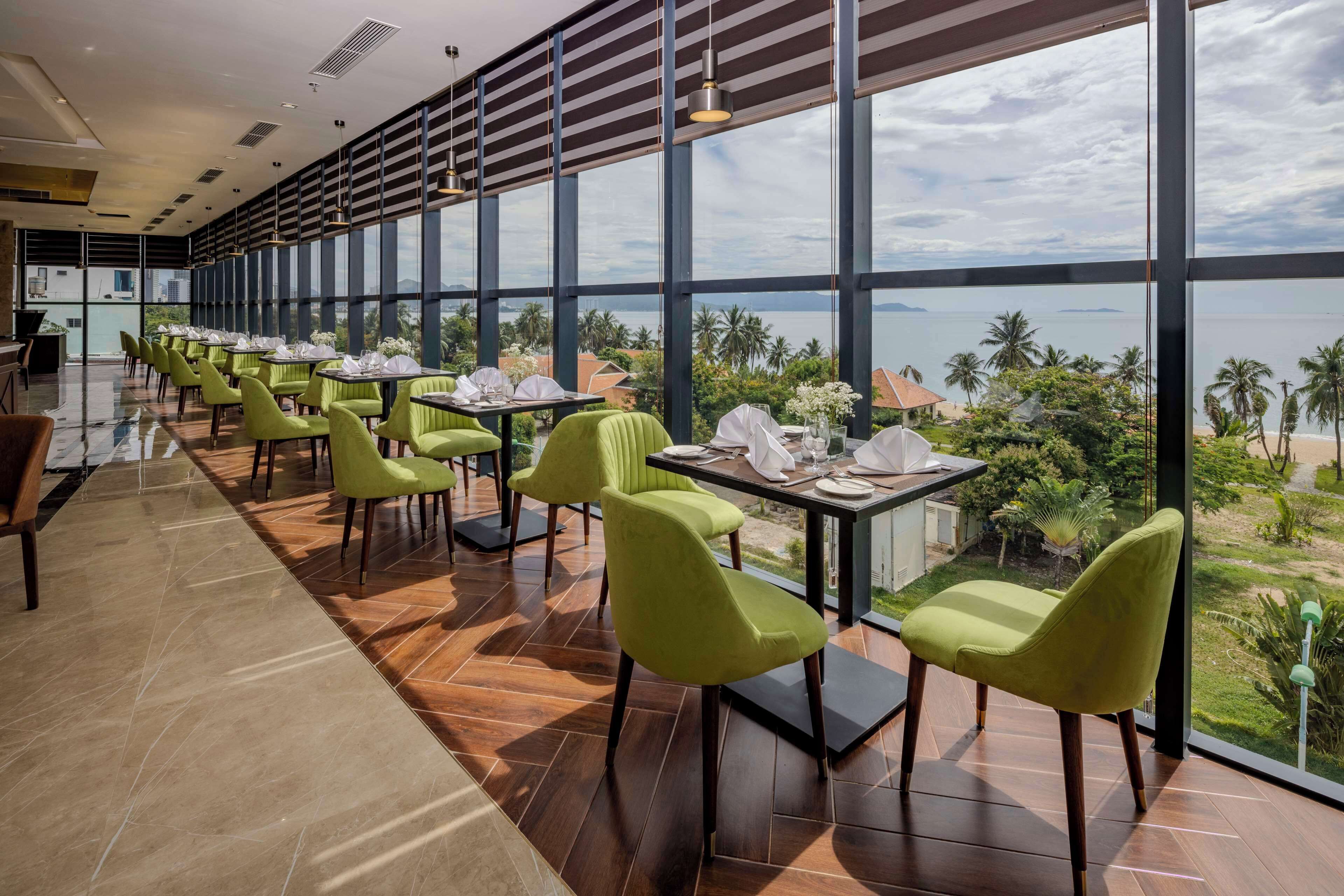 Um restaurante com uma mesa comprida e cadeiras, janelas grandes e vista para o mar.