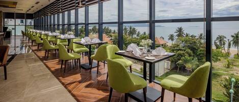 Um restaurante com uma mesa comprida e cadeiras, janelas grandes e vista para o mar.
