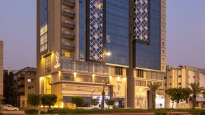 Um hotel moderno com arquitetura vertical e fachada geométrica marcante, várias varandas e sinalização iluminada.