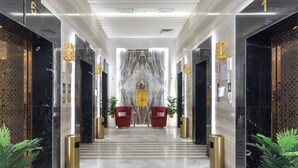 Um lobby de hotel moderno com pisos de mármore, detalhes dourados e cadeiras vermelhas.