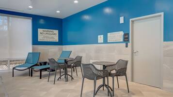 Área da piscina com espreguiçadeiras, uma mesa e uma porta. Um aviso recomenda não nadar sozinho e supervisão para crianças.