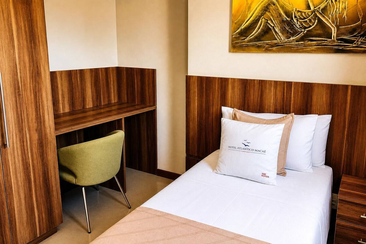 Quarto de hotel com cama, escrivaninha, cadeira e um quadro na parede.