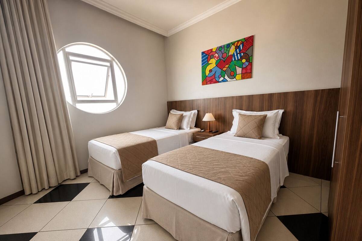Quarto de hotel com duas camas, uma janela, um quadro abstrato colorido e uma cabeceira de madeira.