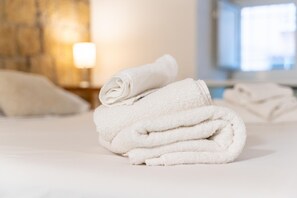 Uma toalha branca e bem dobrada sobre uma cama em quarto de hotel.