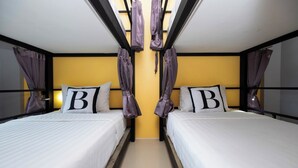 Quarto de hotel com duas camas, cada uma com um travesseiro com uma letra grande.