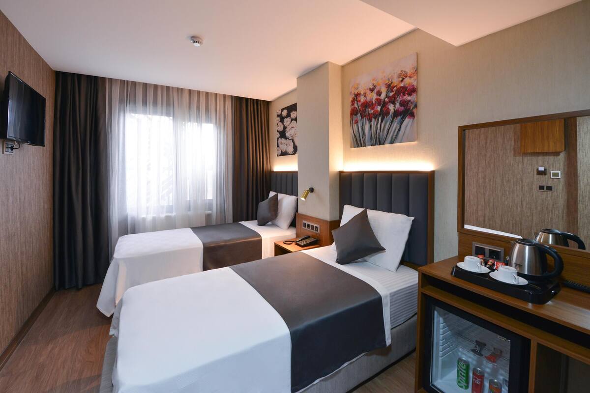 Quarto de hotel com duas camas, um minibar, uma televisão e um quadro na parede.