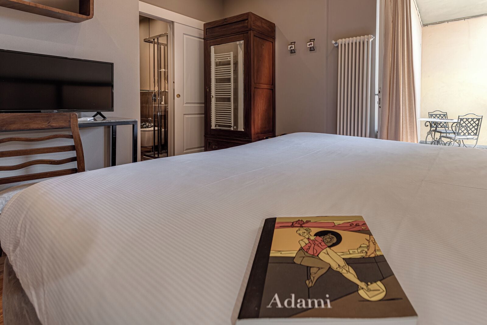 Quarto de hotel com uma cama grande, televisão, guarda-roupa e banheiro visível através de uma porta aberta.