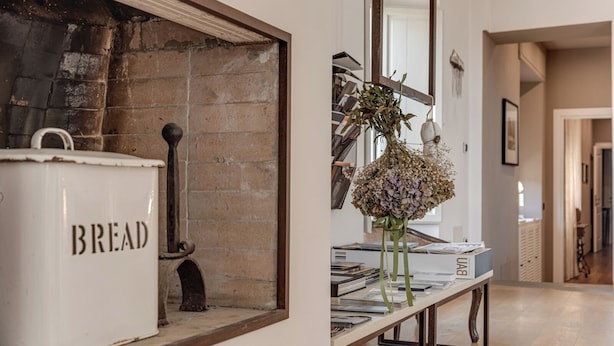 Uma cozinha com um recipiente para pão, uma parede de tijolos rústicos e uma mesa com revistas e um vaso de flores.