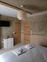 Quarto com uma cama, cômoda, televisão e duas portas de madeira.