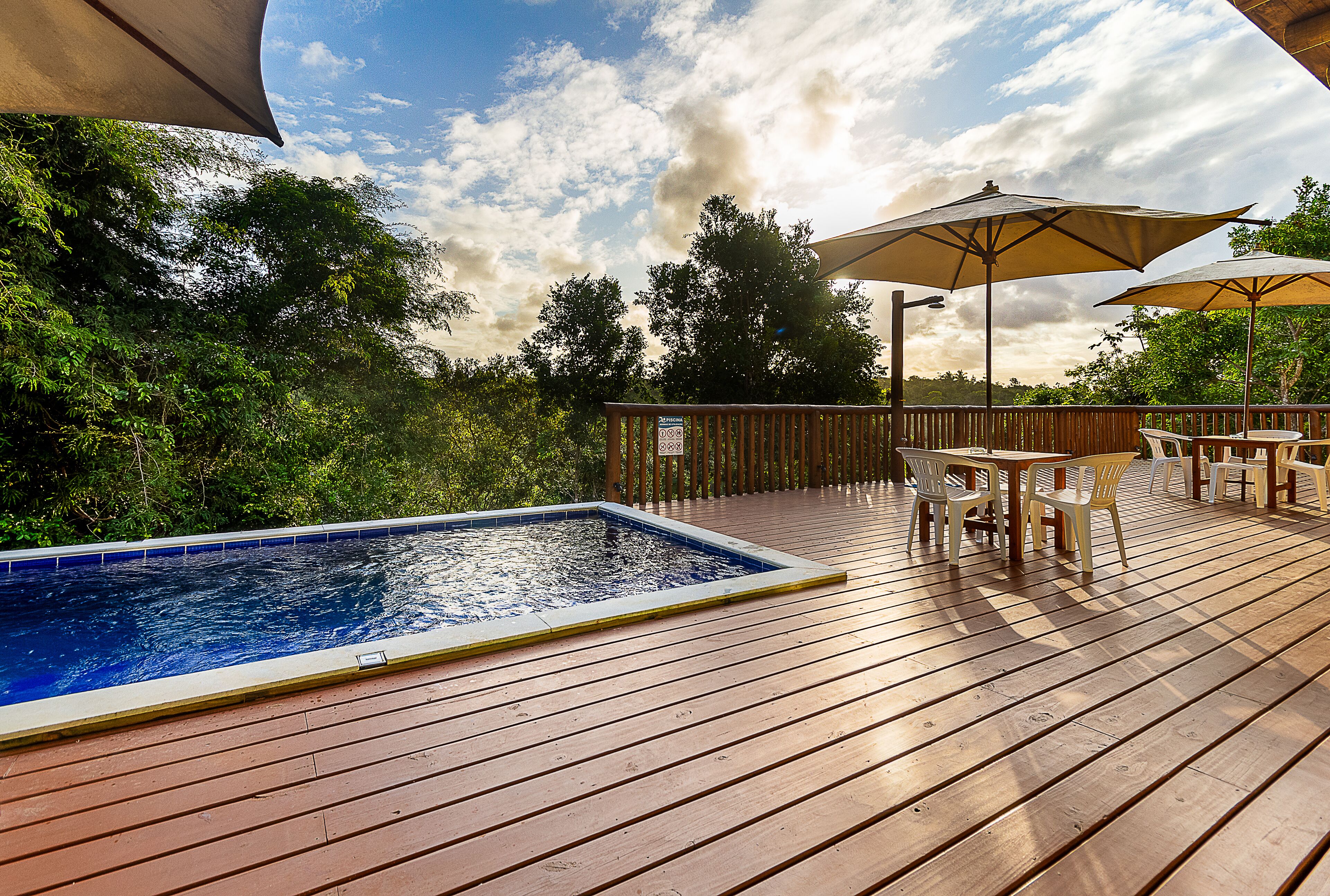 Um deck de madeira com piscina, móveis de exterior e guarda-sóis.