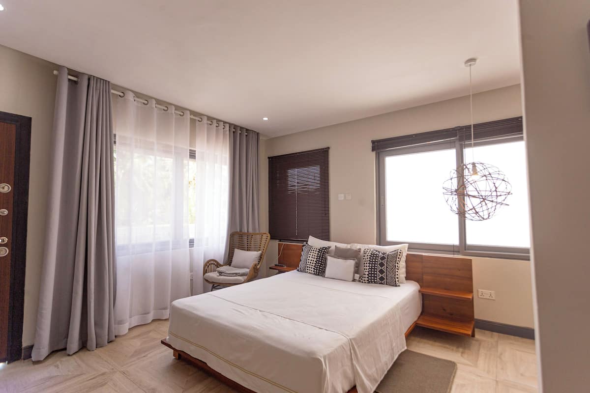 Quarto moderno com uma cama grande, uma cadeira e uma janela com persianas.