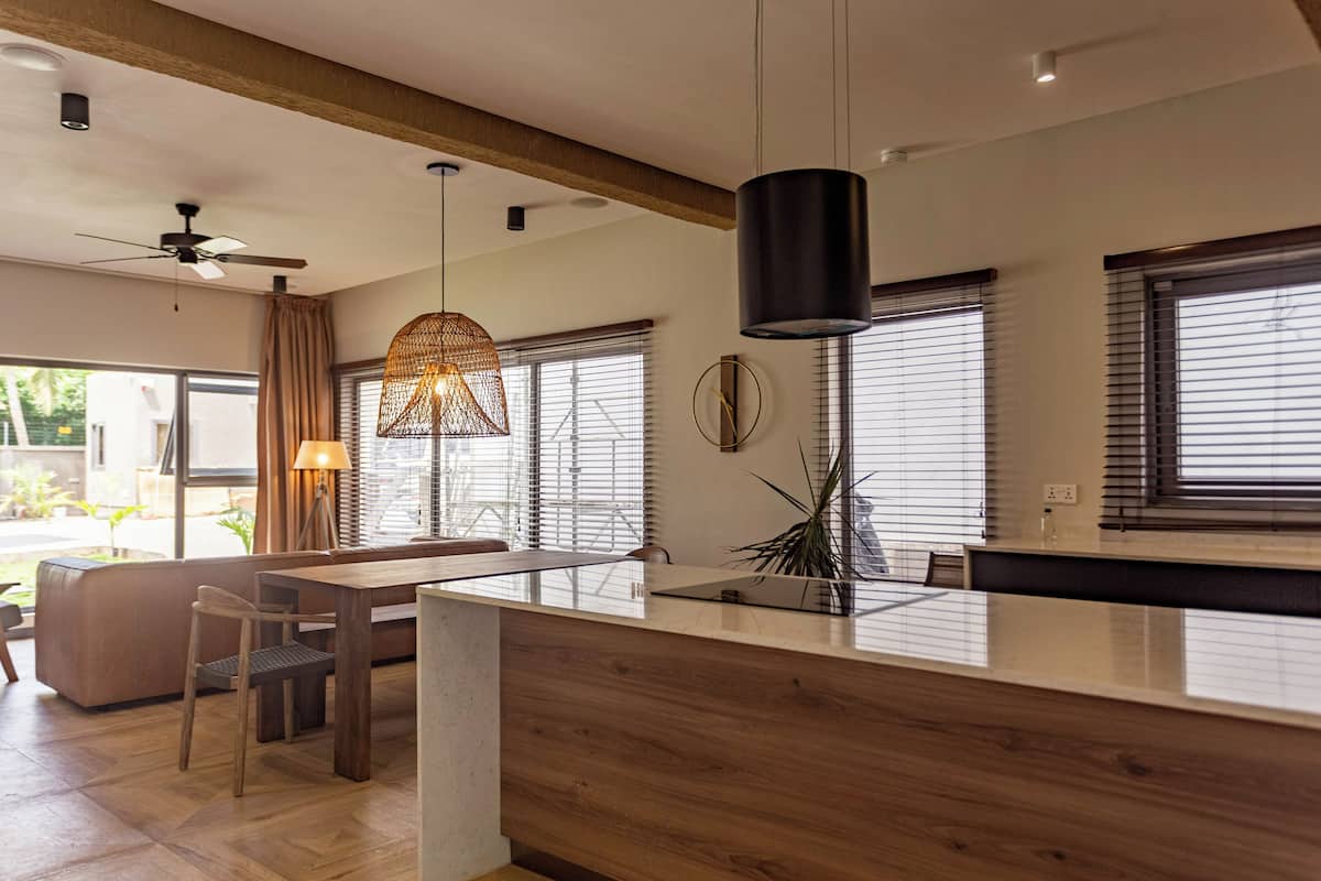 Cozinha moderna com bancadas de madeira, ilha central, luminárias pendentes e grandes janelas com persianas.