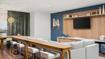 Uma sala de estar moderna com uma mesa de jantar de madeira, banquetas brancas, um sofá cinza e uma TV de tela plana fixada em uma parede de madeira.