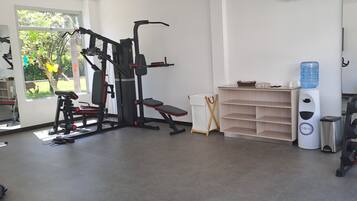 Uma academia com equipamentos de ginástica, bebedouro e um suporte com halteres.