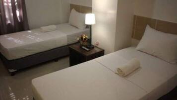 Quarto de hotel com duas camas de solteiro, mesa de cabeceira com abajur e uma pequena mesa com um vaso de flores.