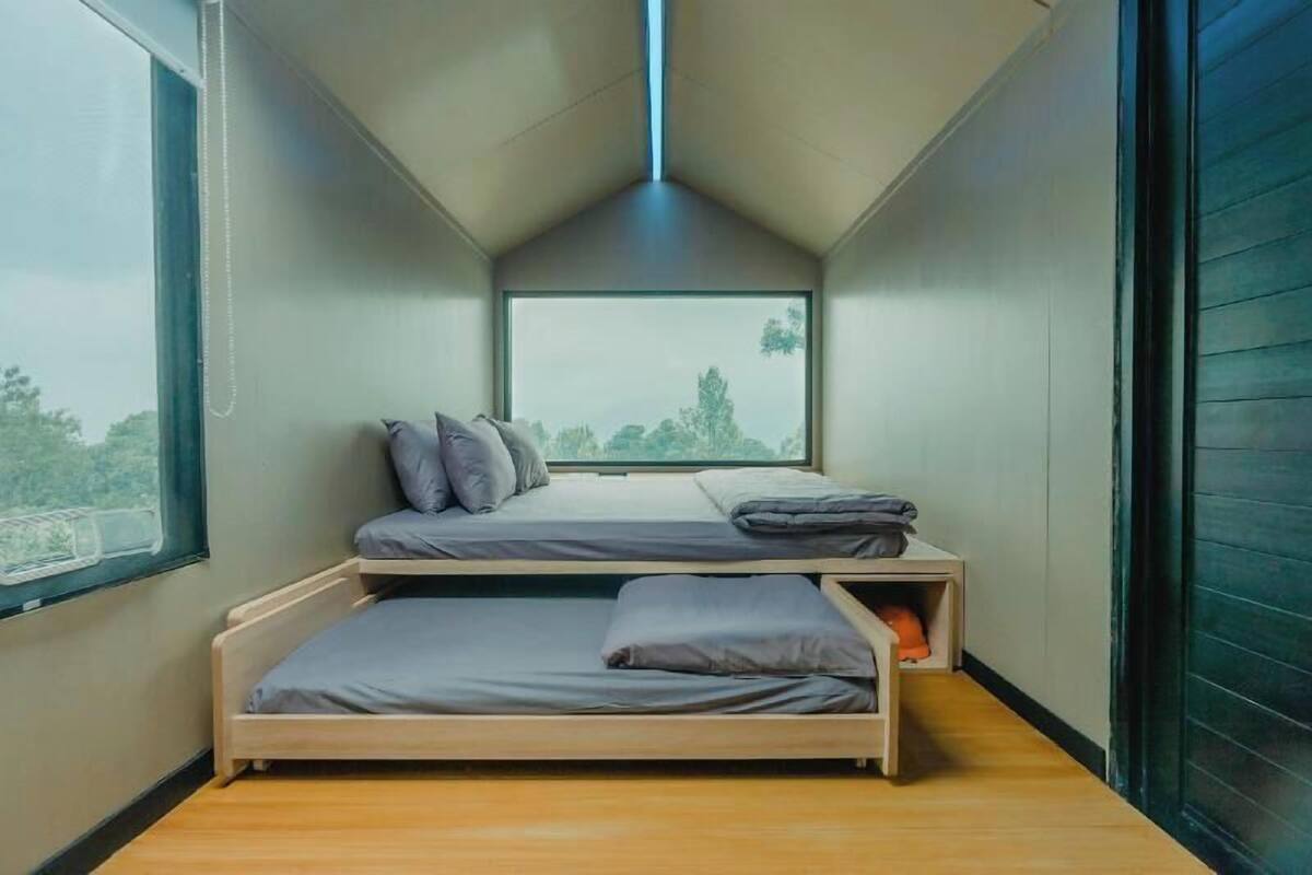 Quarto compacto com duas beliches, uma janela grande e teto inclinado.