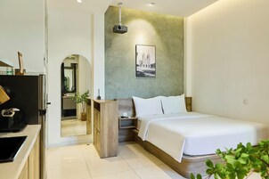 Quarto de hotel moderno com uma cama grande, uma mesa de cabeceira de madeira, uma escrivaninha com computador e um espelho.