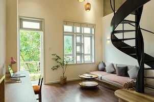 Uma sala de estar moderna com uma escada em espiral, uma escrivaninha de madeira com um laptop, uma mesa redonda e um sofá com almofadas.