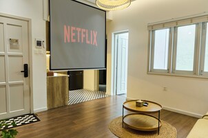 Uma sala de estar moderna com uma grande televisão de tela plana na parede, uma mesa de centro de madeira e um sofá.