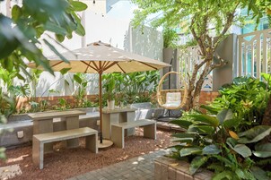 Uma área externa com assentos, incluindo uma mesa de concreto e bancos, rodeada por vegetação exuberante e uma árvore.