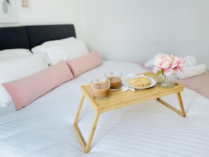 Uma cama com uma bandeja de madeira contendo duas xícaras de café, um prato de biscoitos e um vaso com flores.