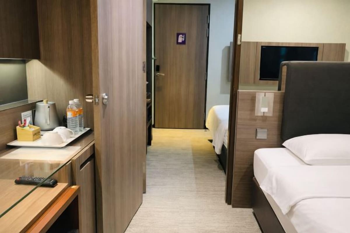 Quarto de hotel com uma cama, uma escrivaninha com computador, televisão e porta do banheiro.