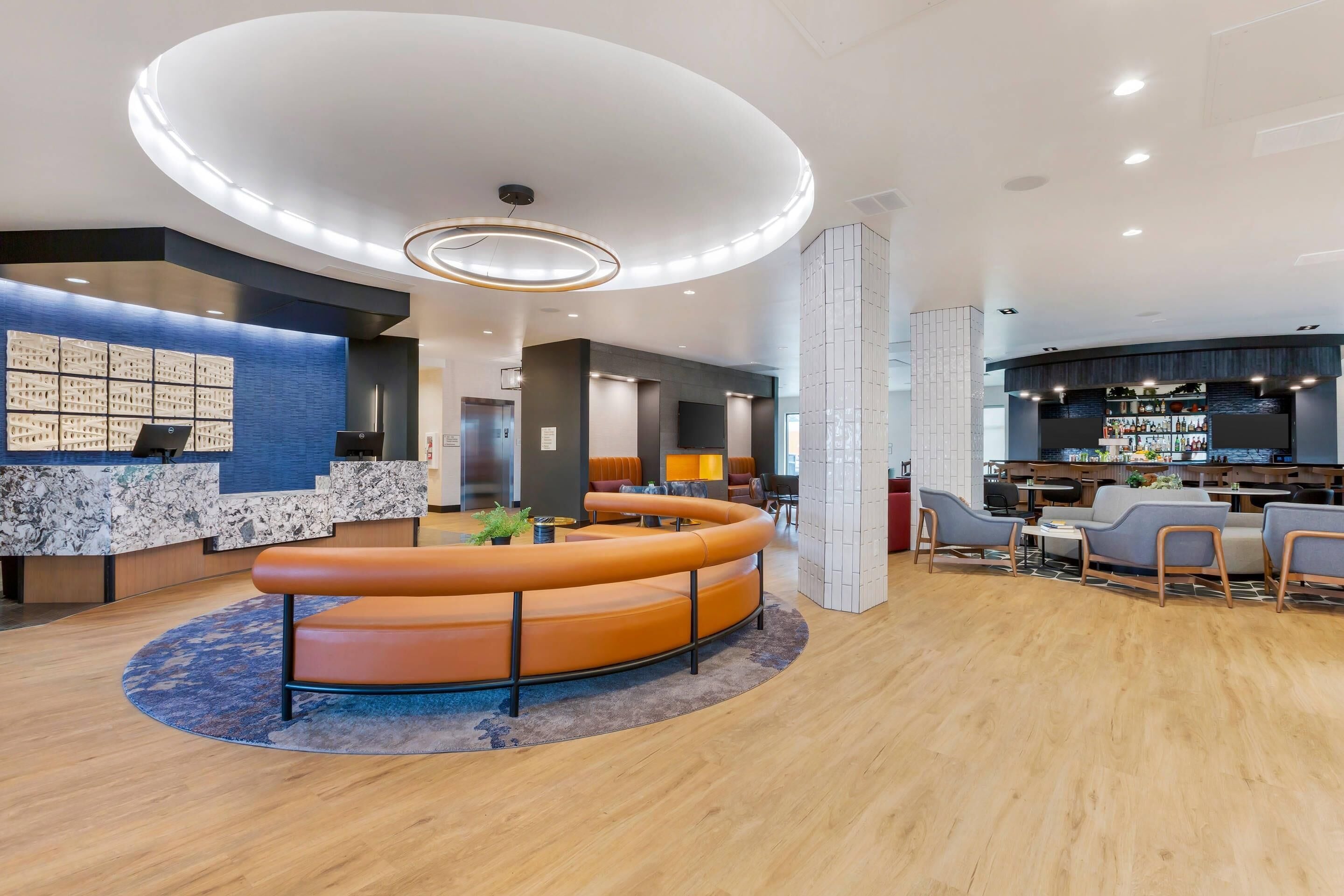 Um lobby moderno de hotel com área de estar em curva, balcão de recepção e zona de bar/lounge.