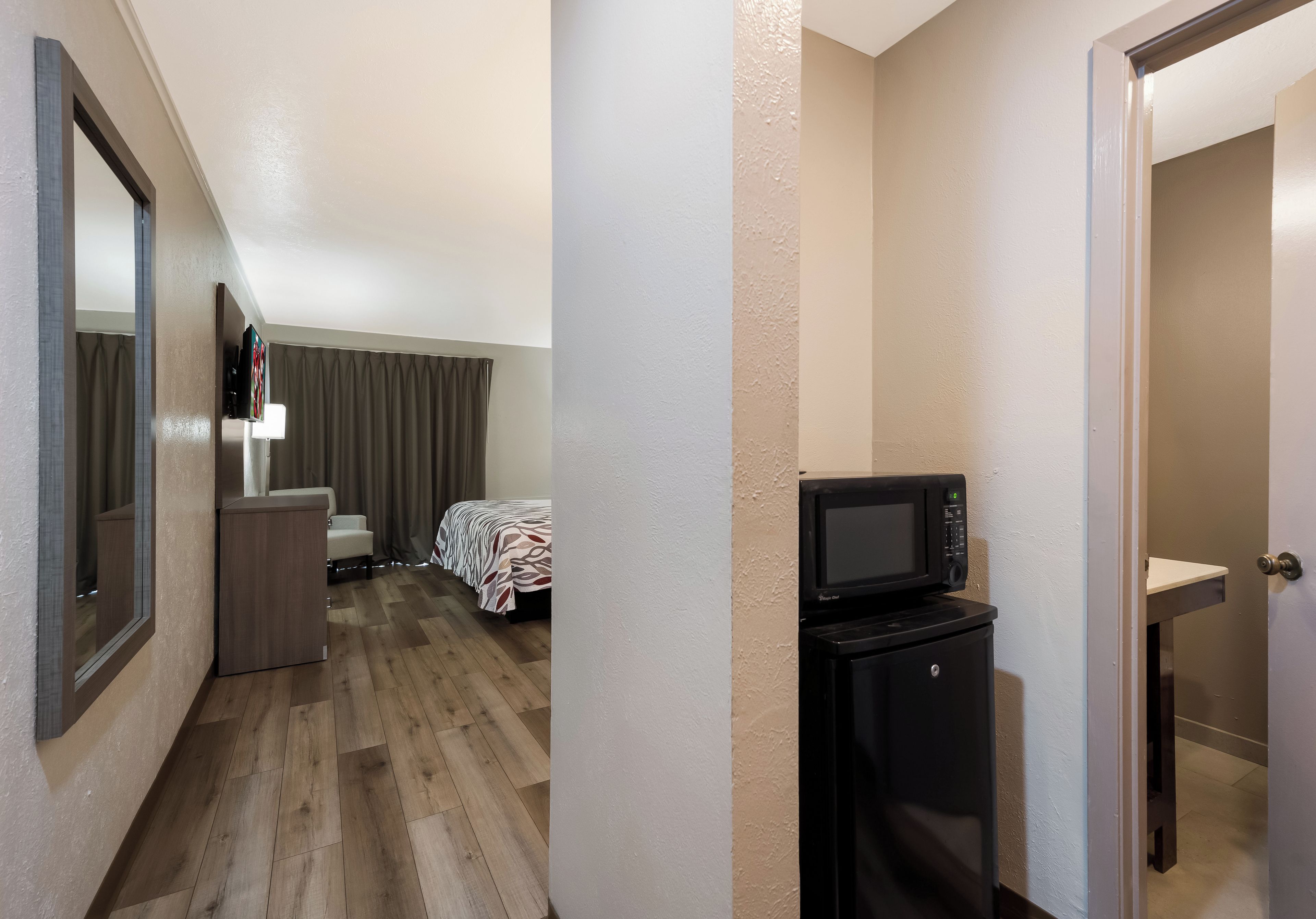 Quarto de hotel com uma cama, uma escrivaninha, uma televisão e um micro-ondas.