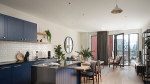 Uma cozinha moderna com armários azul escuro, uma ilha central e um espaço de jantar com cadeiras de madeira.