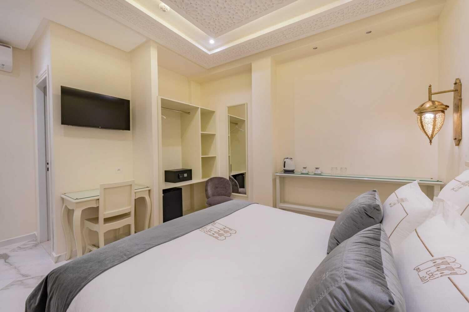 Quarto de hotel com cama, escrivaninha, cadeira, televisão e minibar.