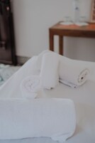 Cama com toalhas brancas dobradas e mesa de cabeceira de madeira com garrafa e copos.