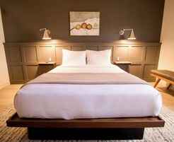 Uma cama grande com estrutura de madeira, duas mesas de cabeceira e uma luminária fixada na parede.