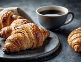 Croissants e uma chávena de café sobre uma superfície escura.