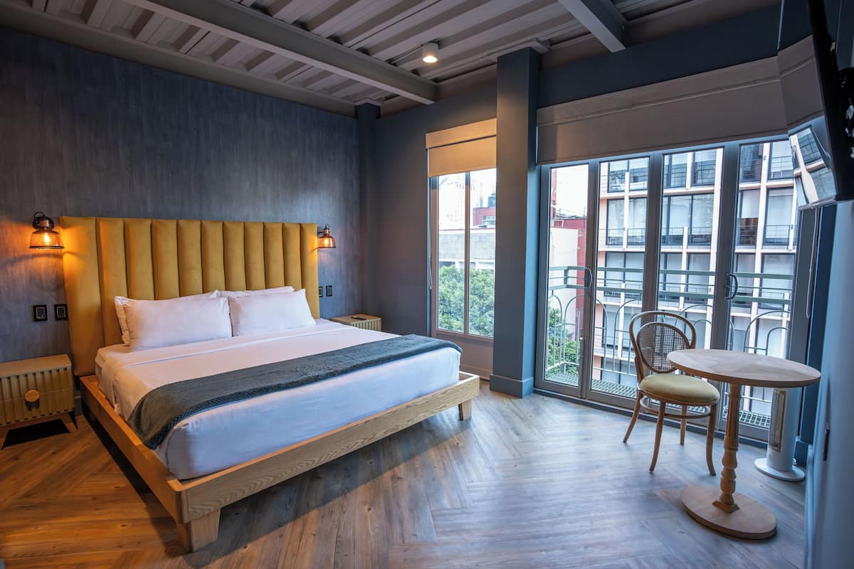 Quarto com cama grande, luminárias de cabeceira, piso de madeira, mesa redonda e uma cadeira.