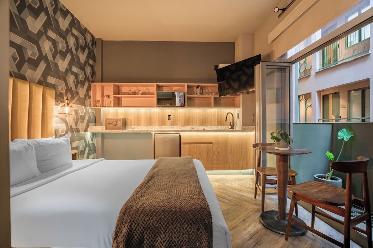 Quarto de hotel pequeno com cama, mesa de cabeceira e uma kitchenette.