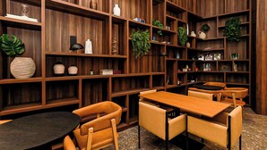 Uma biblioteca com estantes de madeira, uma mesa redonda e várias cadeiras.