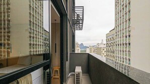 Uma varanda estreita com vista para edifícios da cidade e uma montanha ao longe.