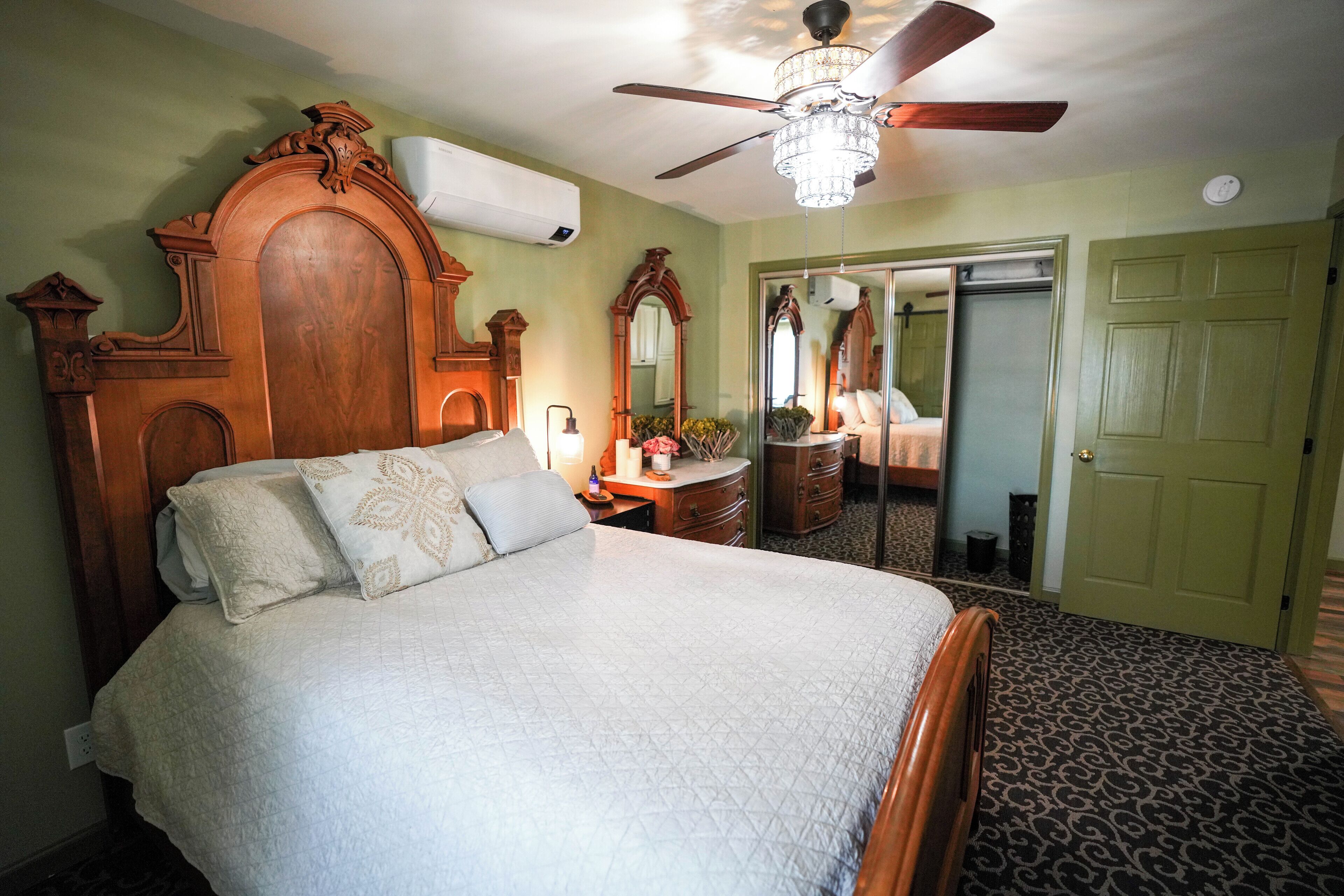 Quarto com cama grande, cabeceira de madeira, ventilador de teto e espelho.