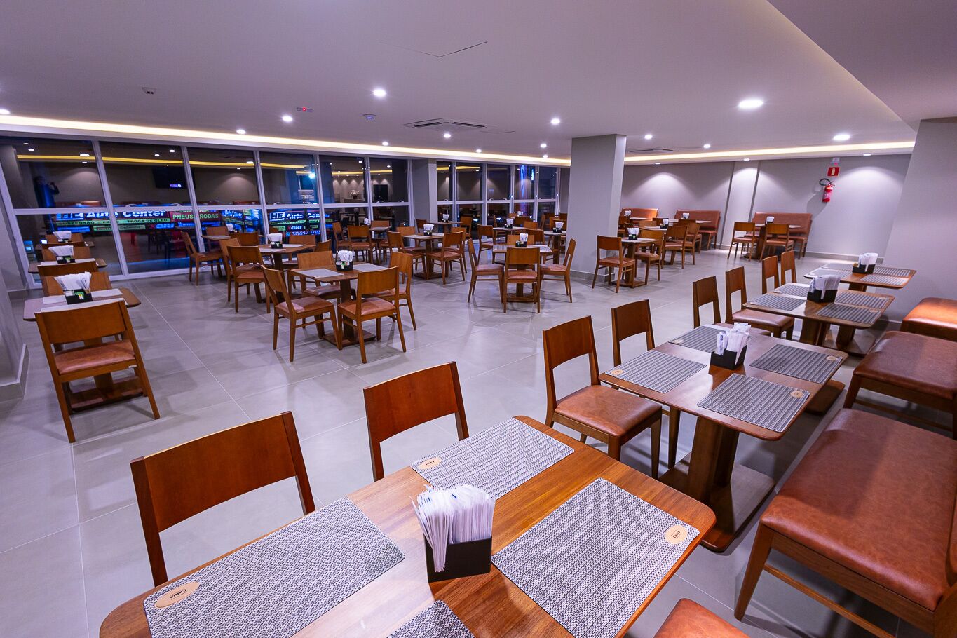 Um restaurante espaçoso com várias mesas e cadeiras, grandes janelas e um design de interiores moderno.