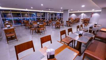 Um restaurante espaçoso com várias mesas e cadeiras, grandes janelas e um design de interiores moderno.